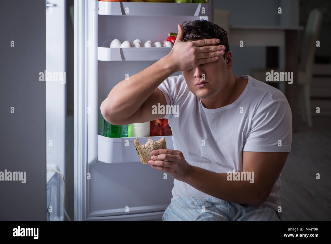 Man at the fridge eating at night Stock Photo - Alamy