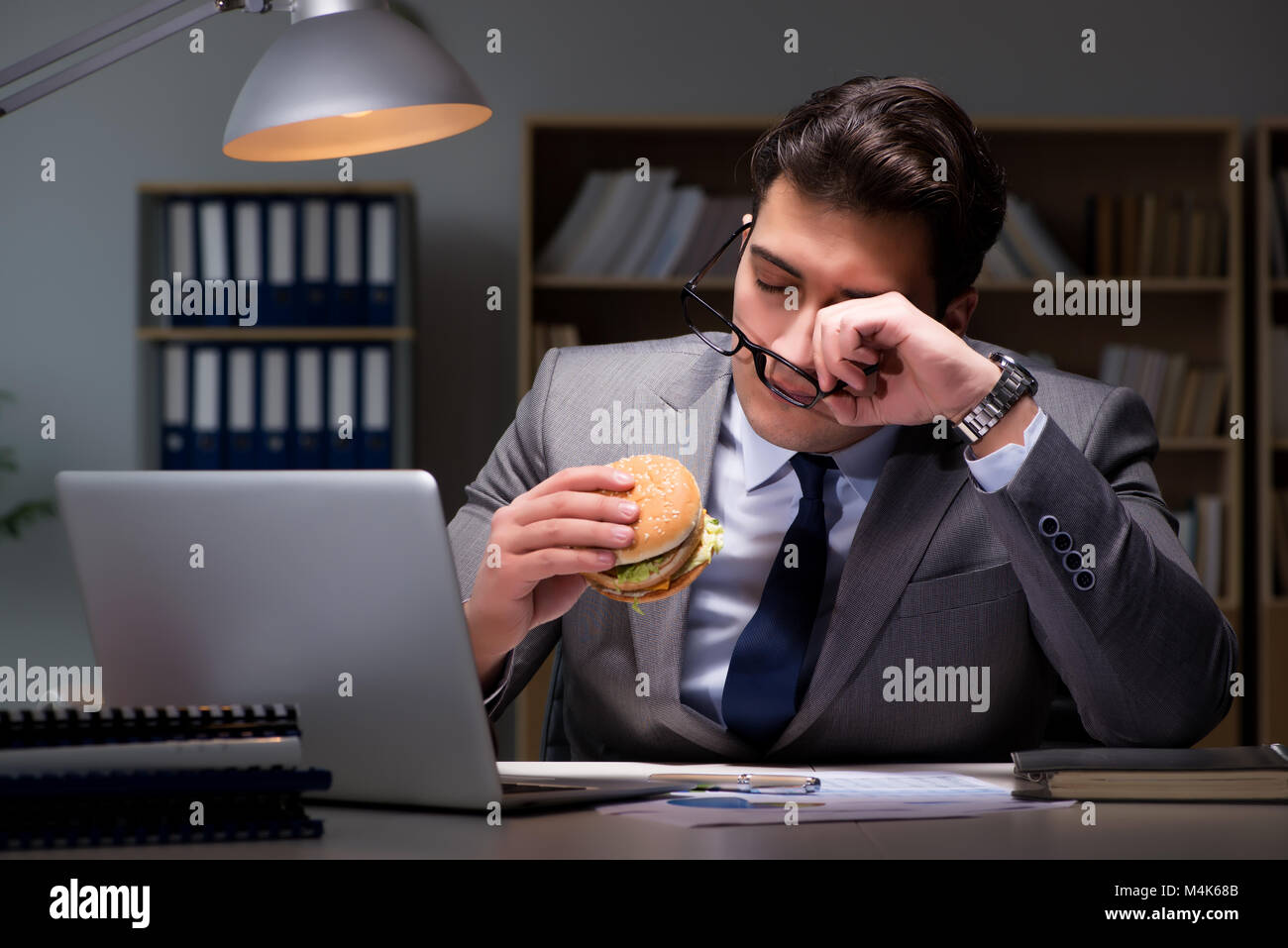 Businessman late at night eating a burger Stock Photo - Alamy