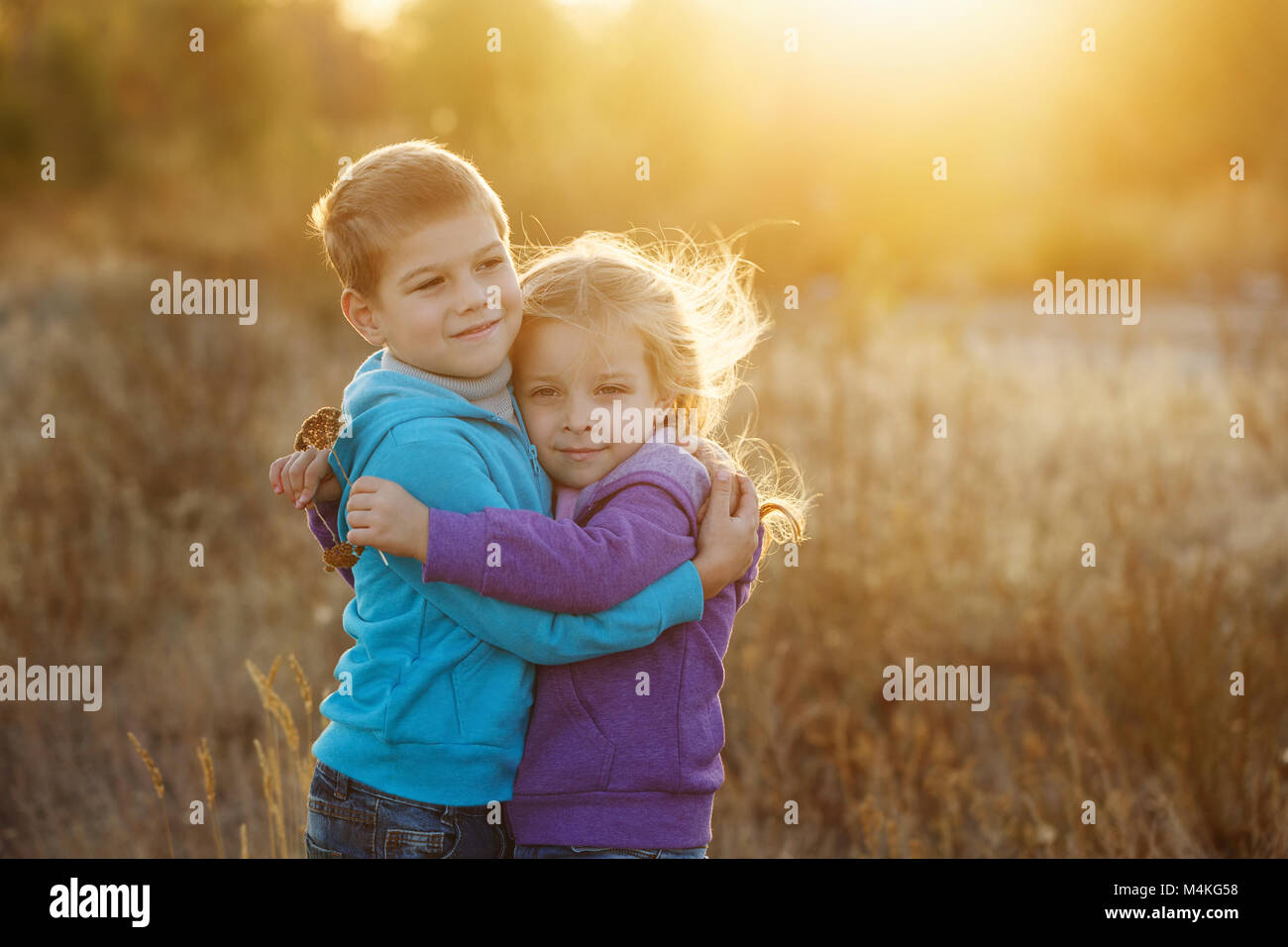 Family time. Brother and sister embrace on a golden meadow in the rays ...