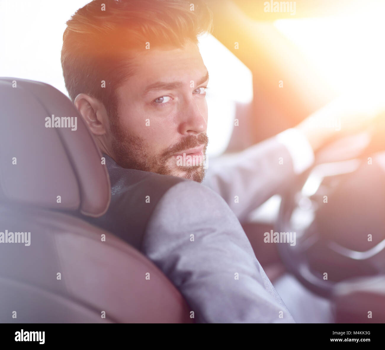 handsome man looking at camera sitting in a car, view from rear seat ...