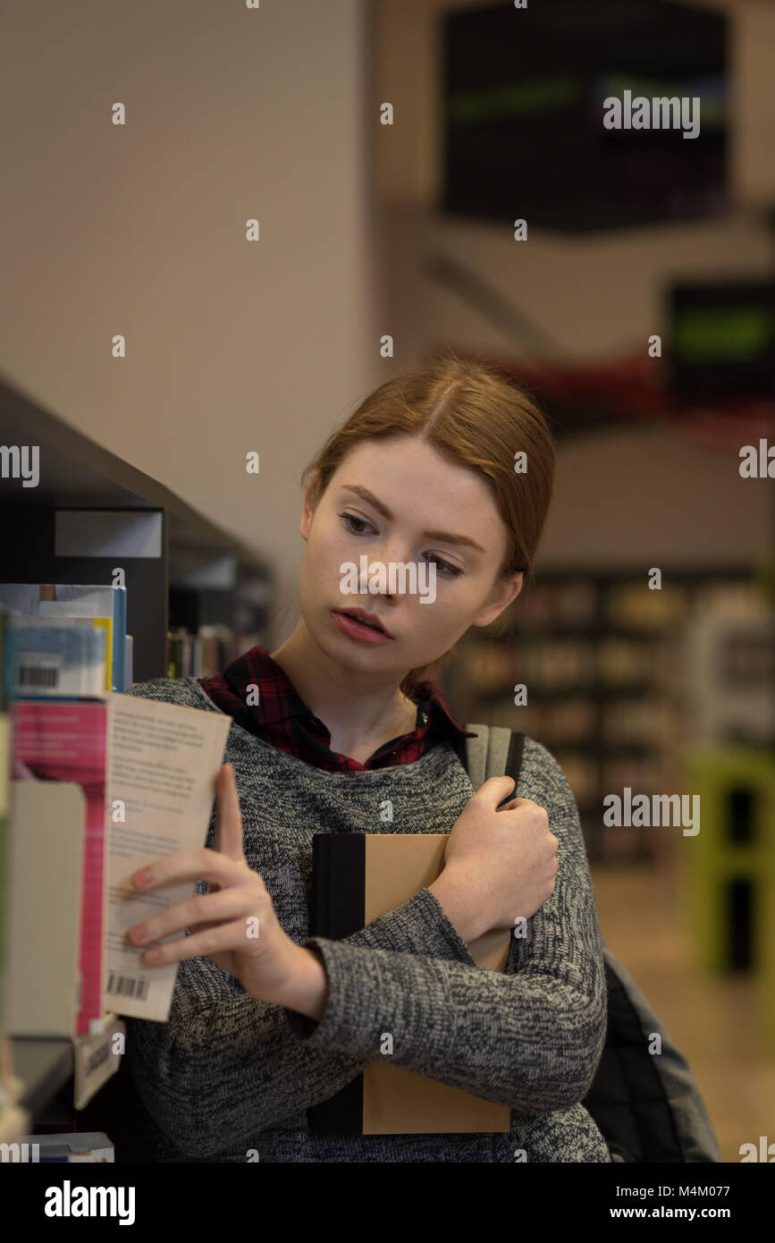 Young woman picking up a book from the bookshelf Stock Photo - Alamy
