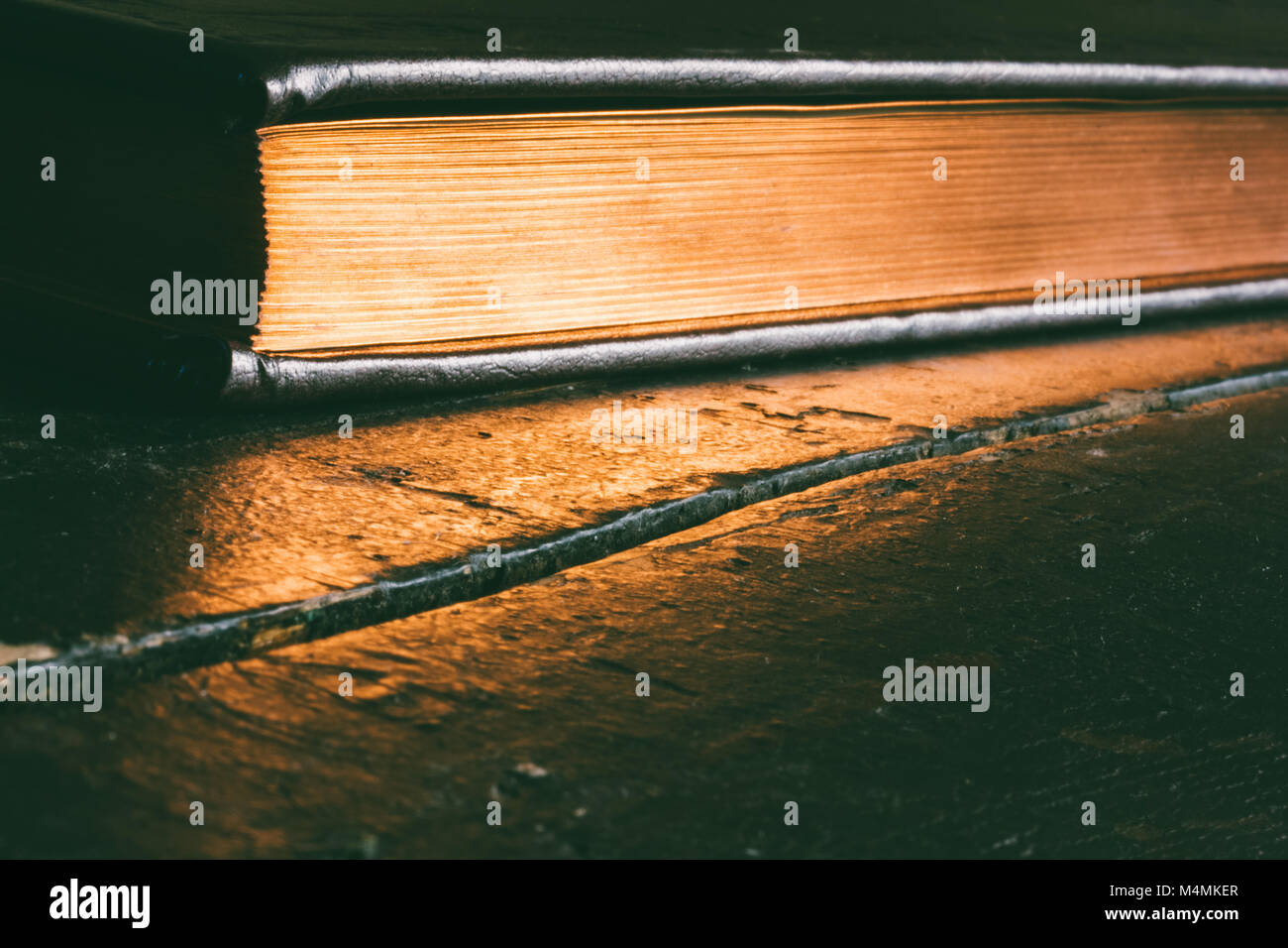 A closed book with a Golden edge on an old black wooden table with copy ...