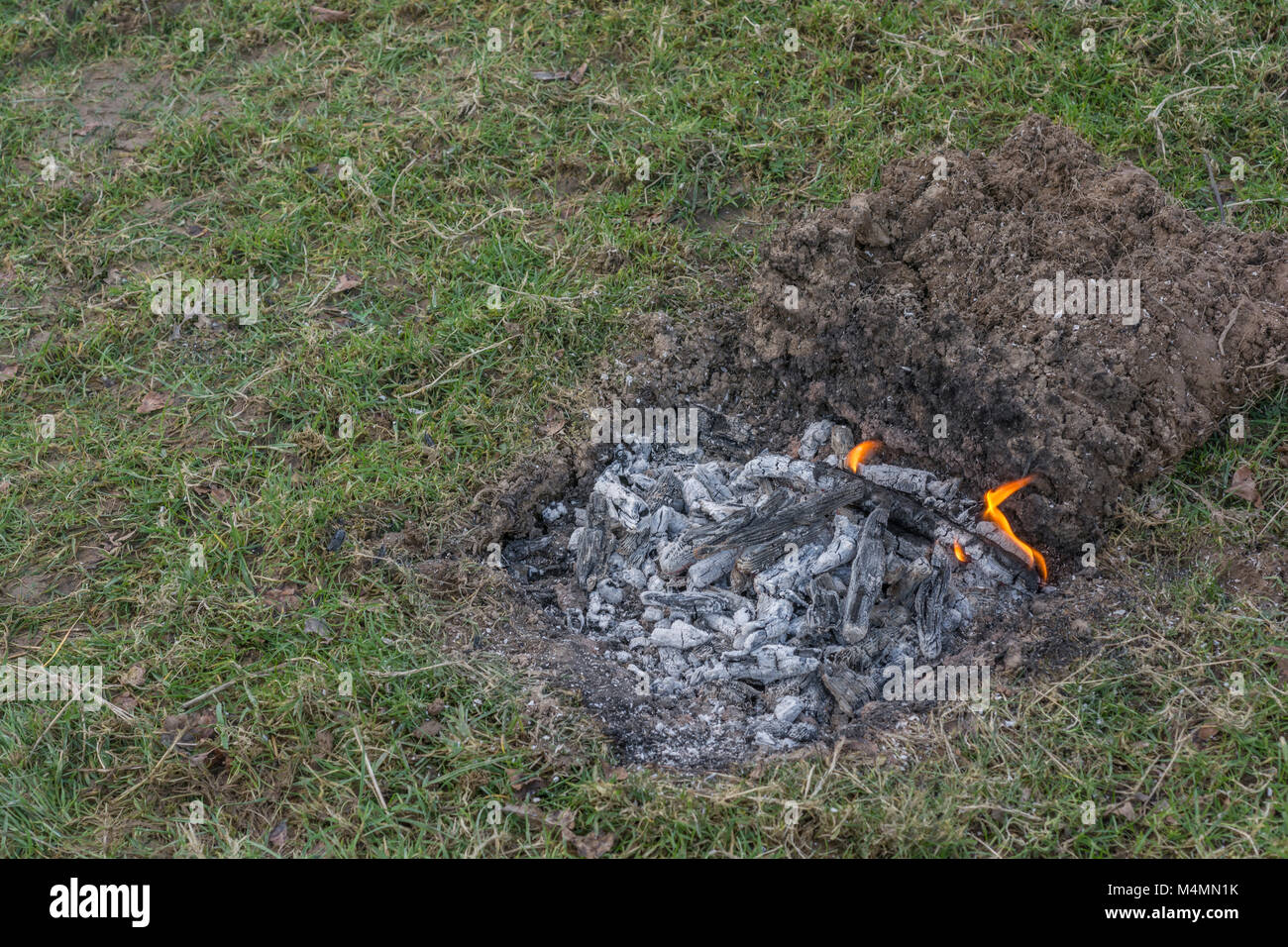 Grass turf cut away to form a shallow pit for a covert survival fire ...