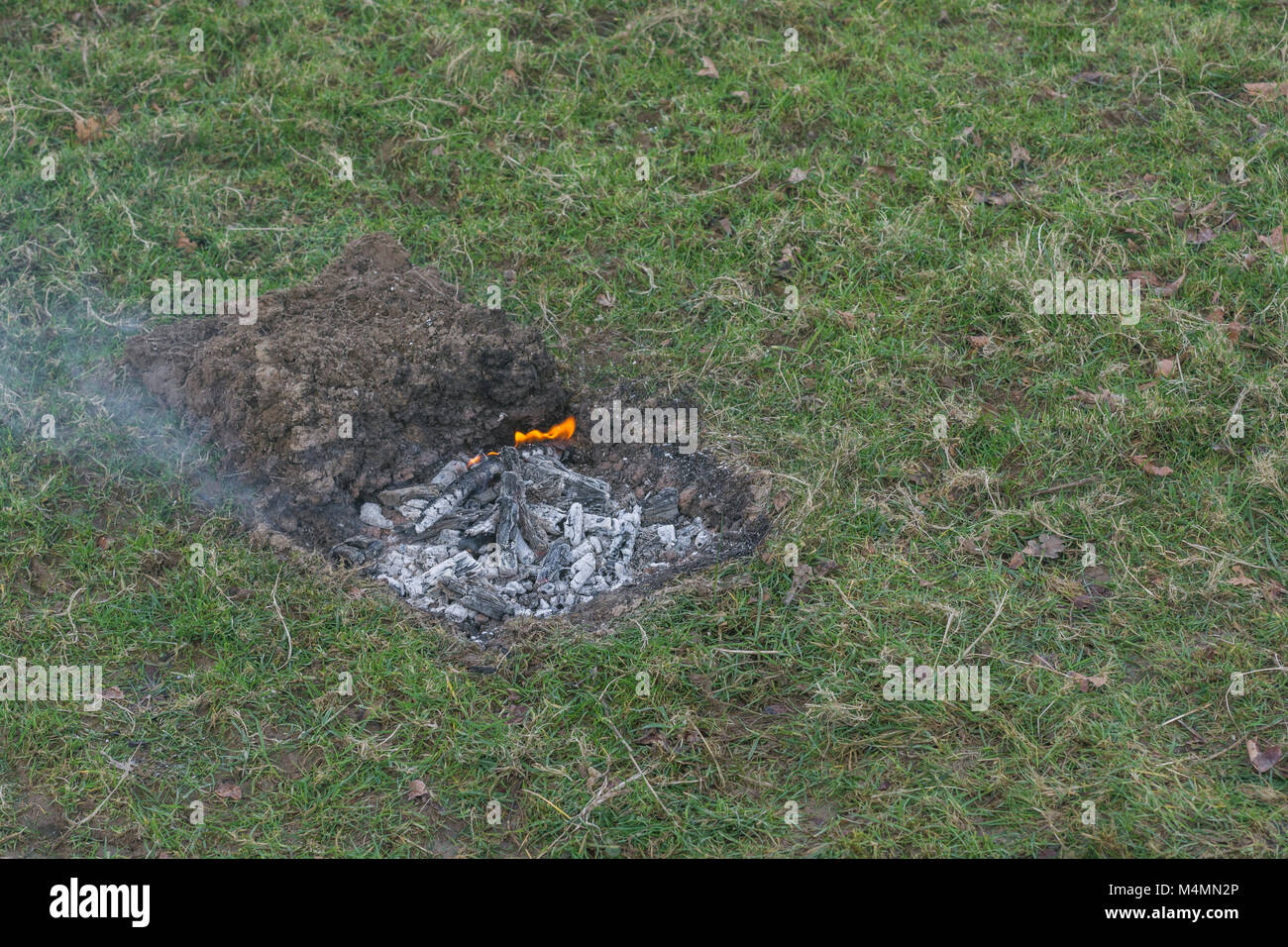 Grass turf cut away to form a shallow pit for a covert survival fire ...