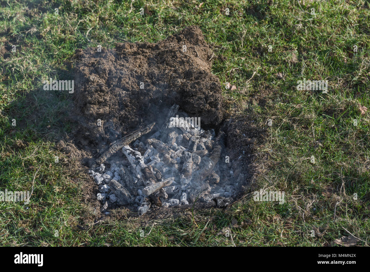 Grass turf cut away to form a shallow pit for a covert survival fire ...