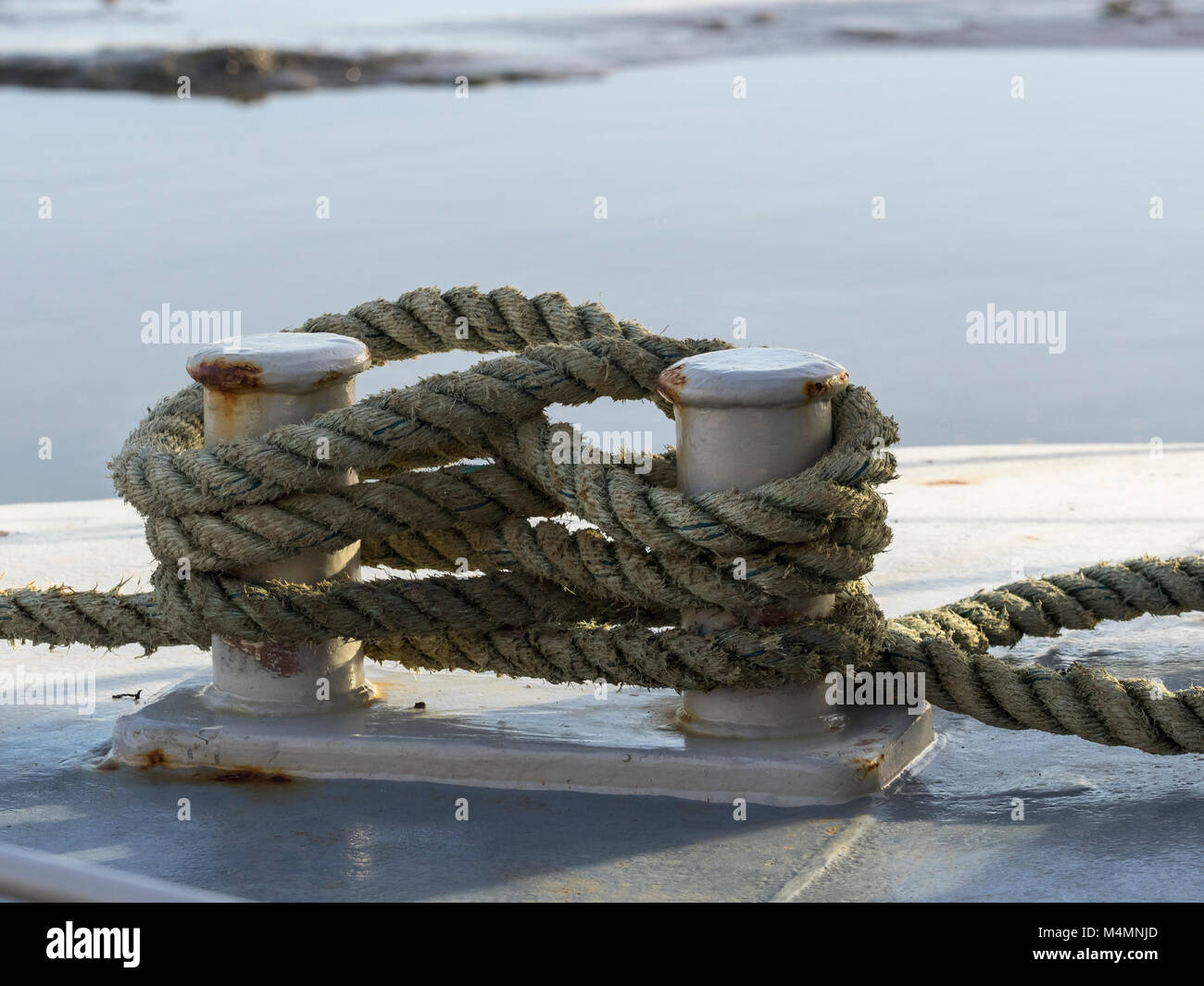 Closeup of old worn rope on steel cleat on quayside with sea in the ...