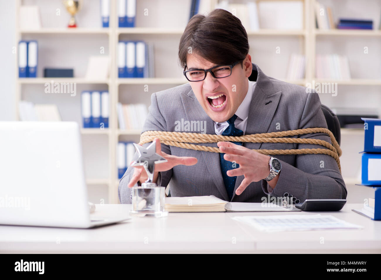 Businessman tied up with rope in office Stock Photo - Alamy