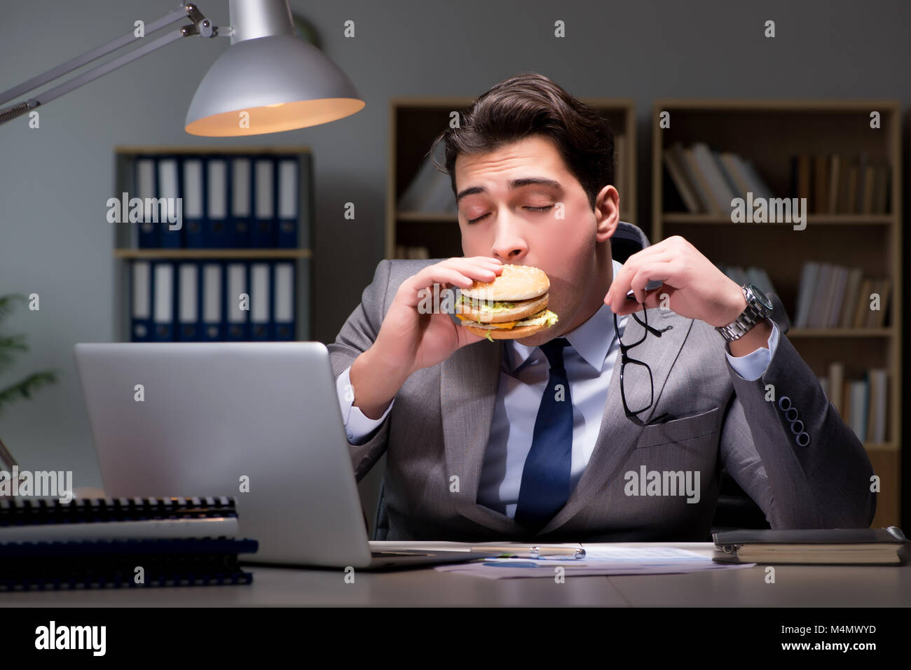 Businessman late at night eating a burger Stock Photo - Alamy