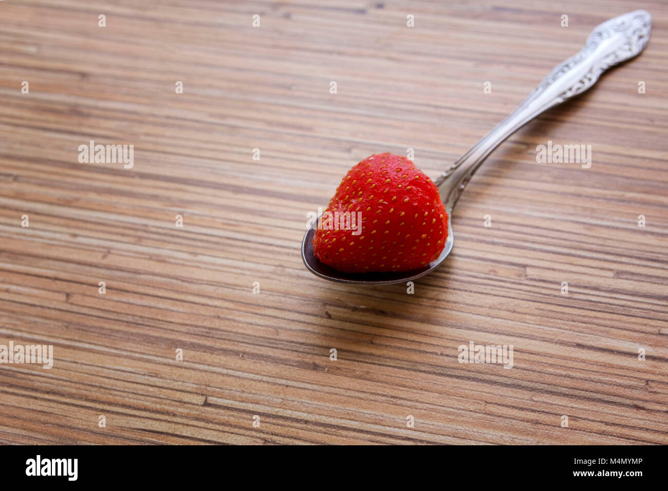 A single strawberry in small spoonl on wooden table background Stock ...
