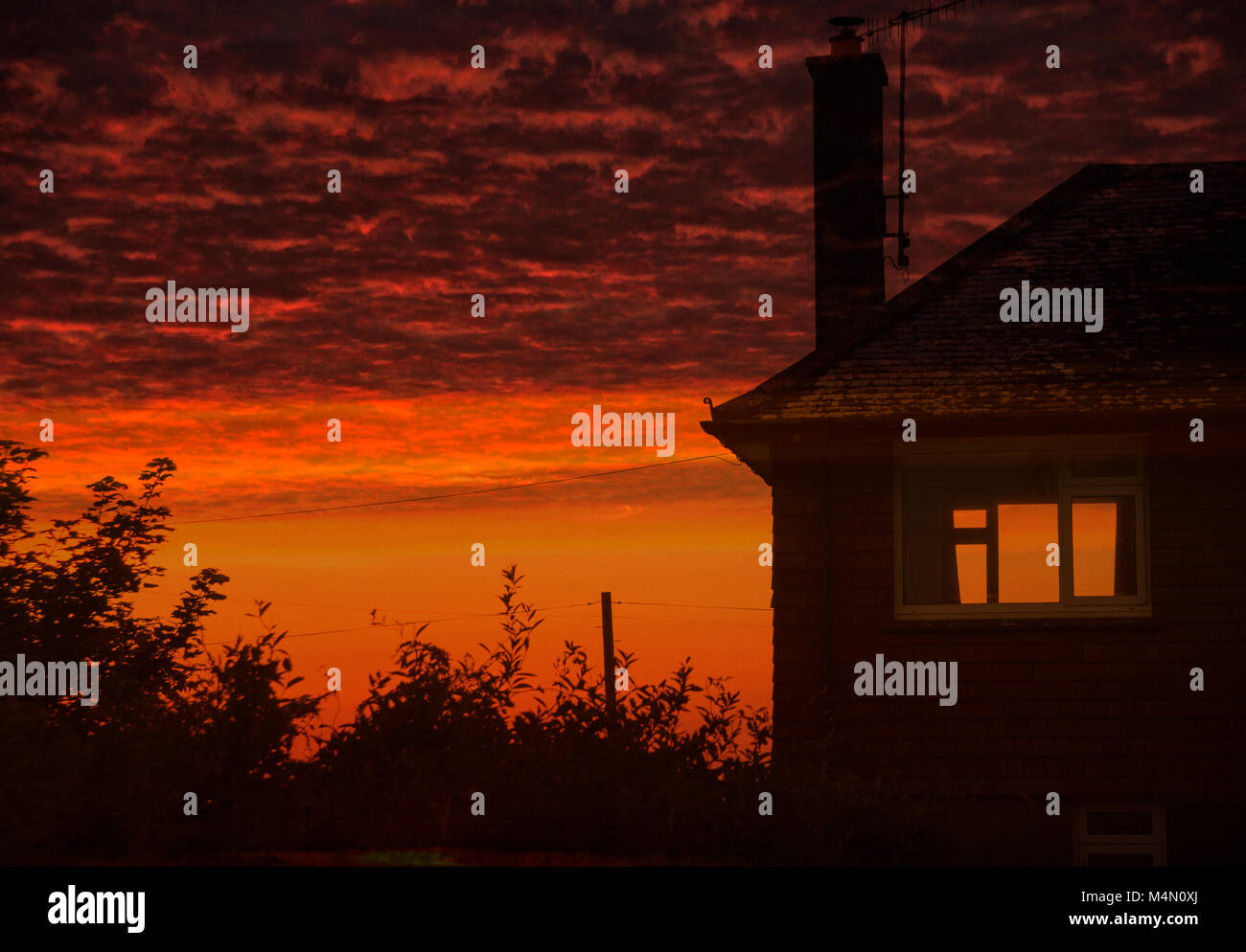 Fiery red sunset sky with clouds and a single house Stock Photo - Alamy