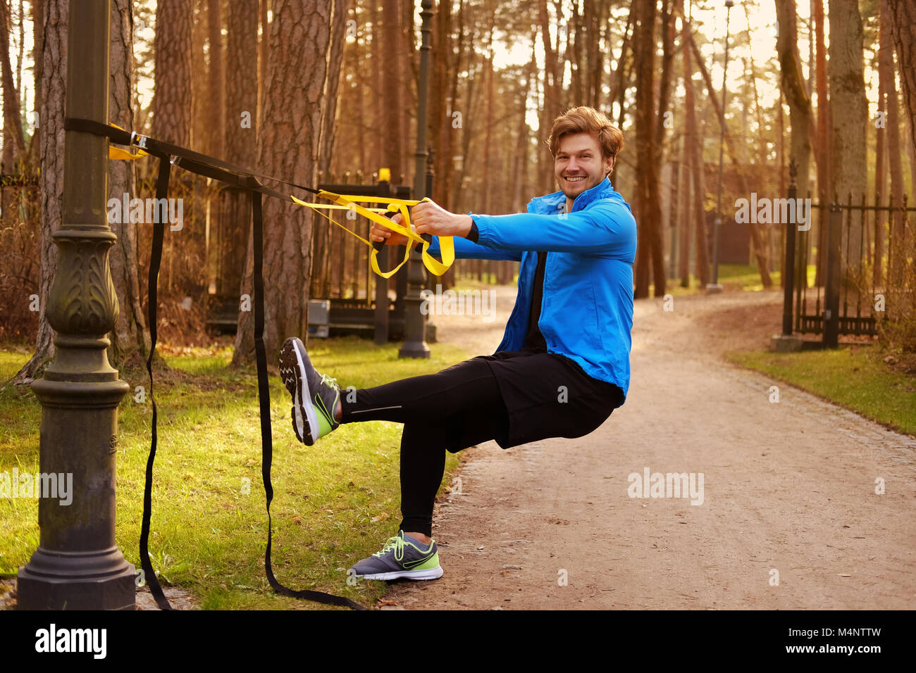 Attractive sporty male exercising with fitness trx strips in a park ...