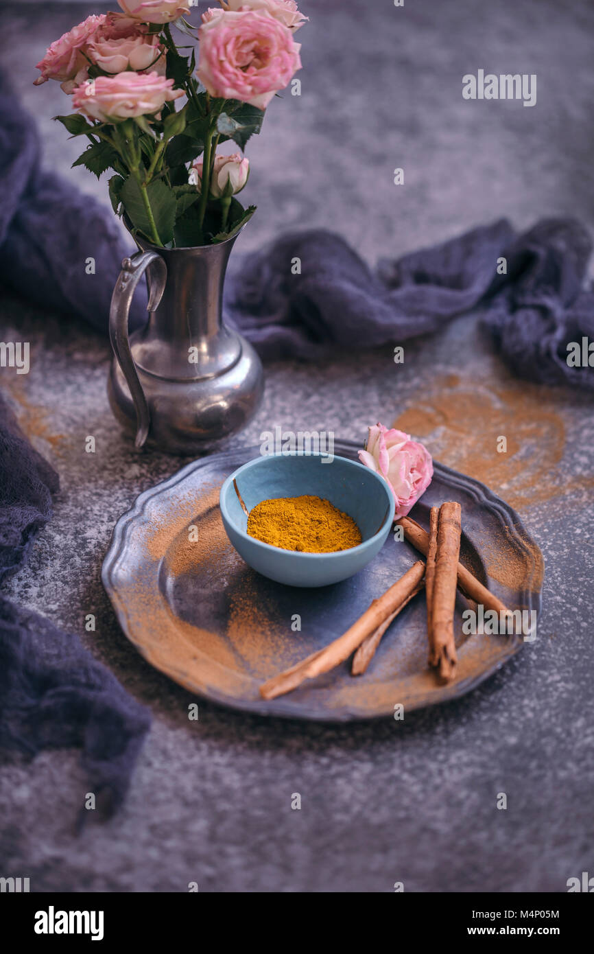Turmeric powder in a small blue bowl and cinnamon sticks on a grey ...