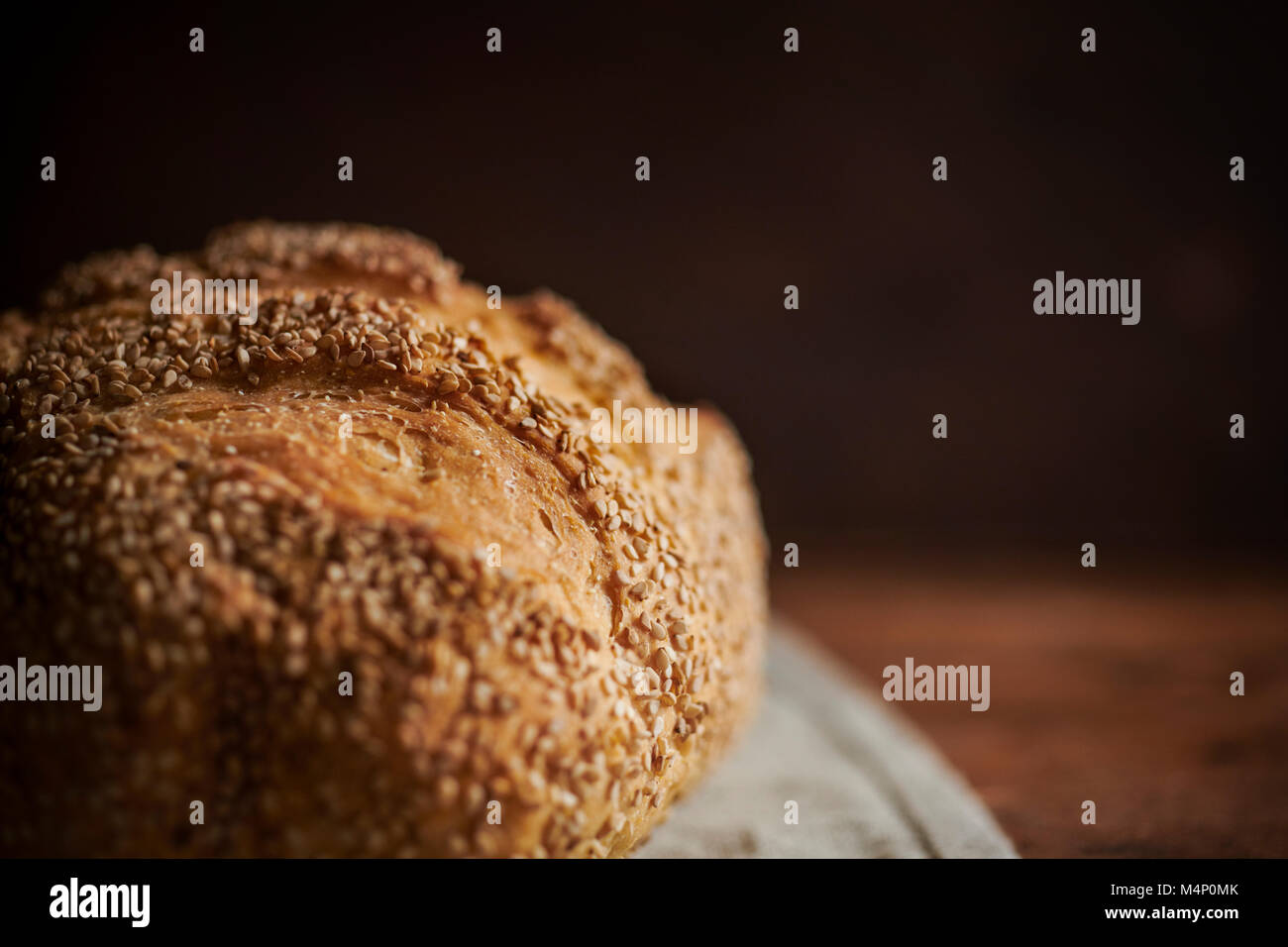 A close, detail shot of a loaf of sesame bread on a rich wood surface ...