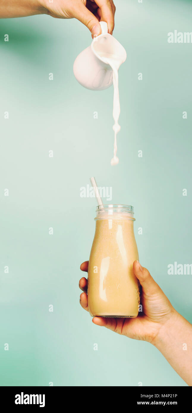 Womans hand holding smoothie shake against bright wall. Pouring milk ...