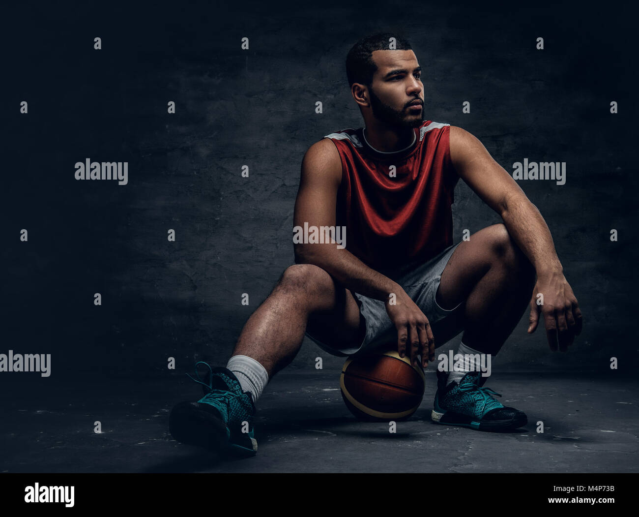 Full body portrait of a black basketball player sits on a floor and ...