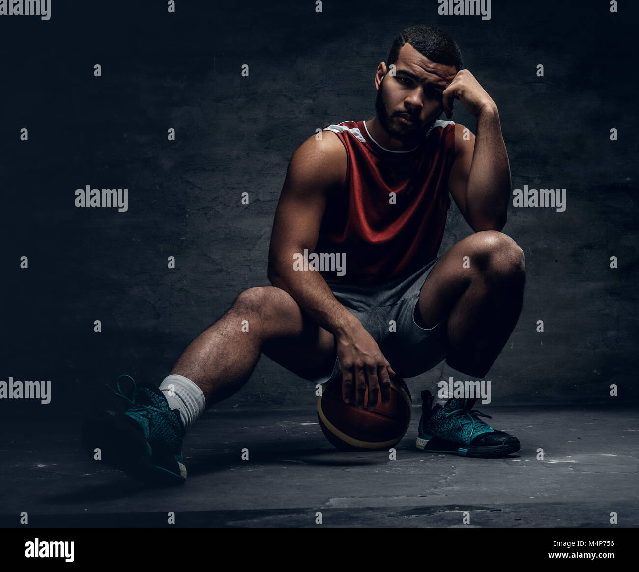Full body portrait of a black basketball player sits on a floor and ...
