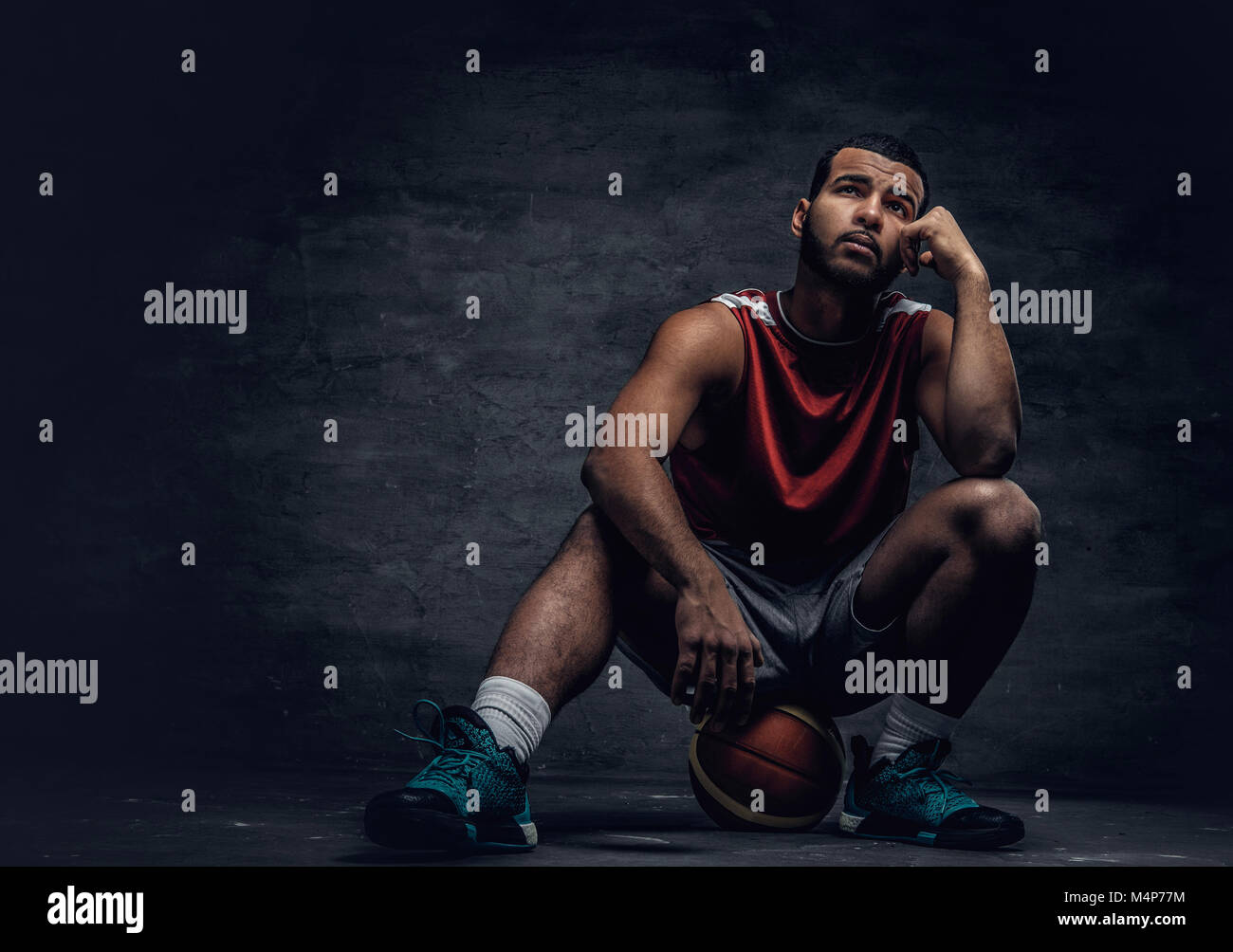 Full body portrait of a black basketball player sits on a floor and ...