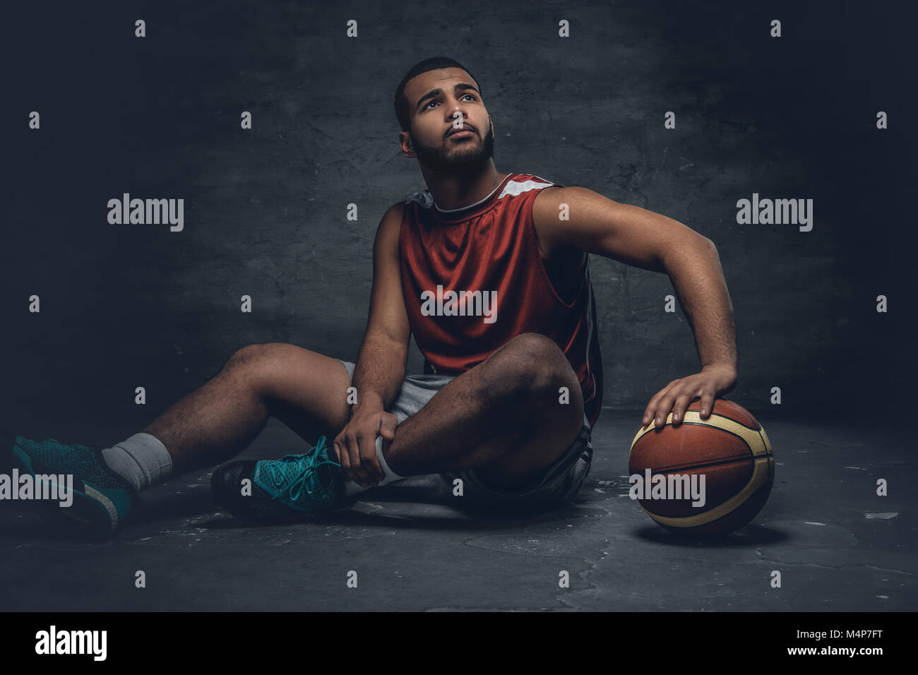 Full body portrait of a black basketball player sits on a floor and ...