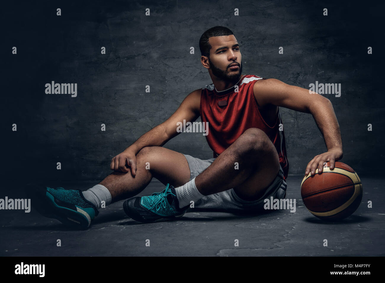 Full body portrait of a black basketball player sits on a floor and ...