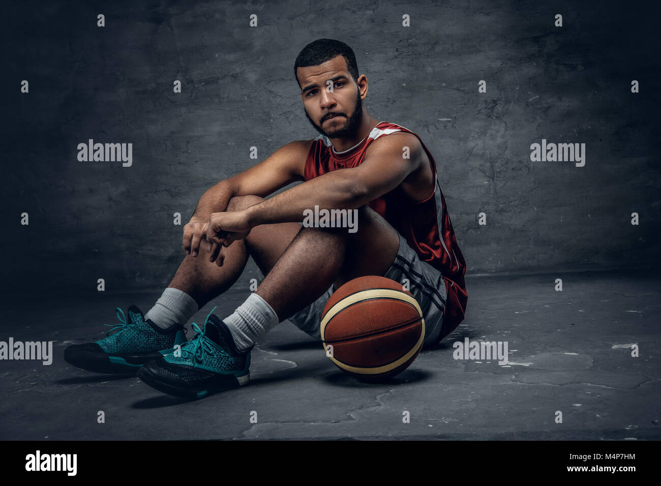 Full body portrait of a black basketball player sits on a floor and ...