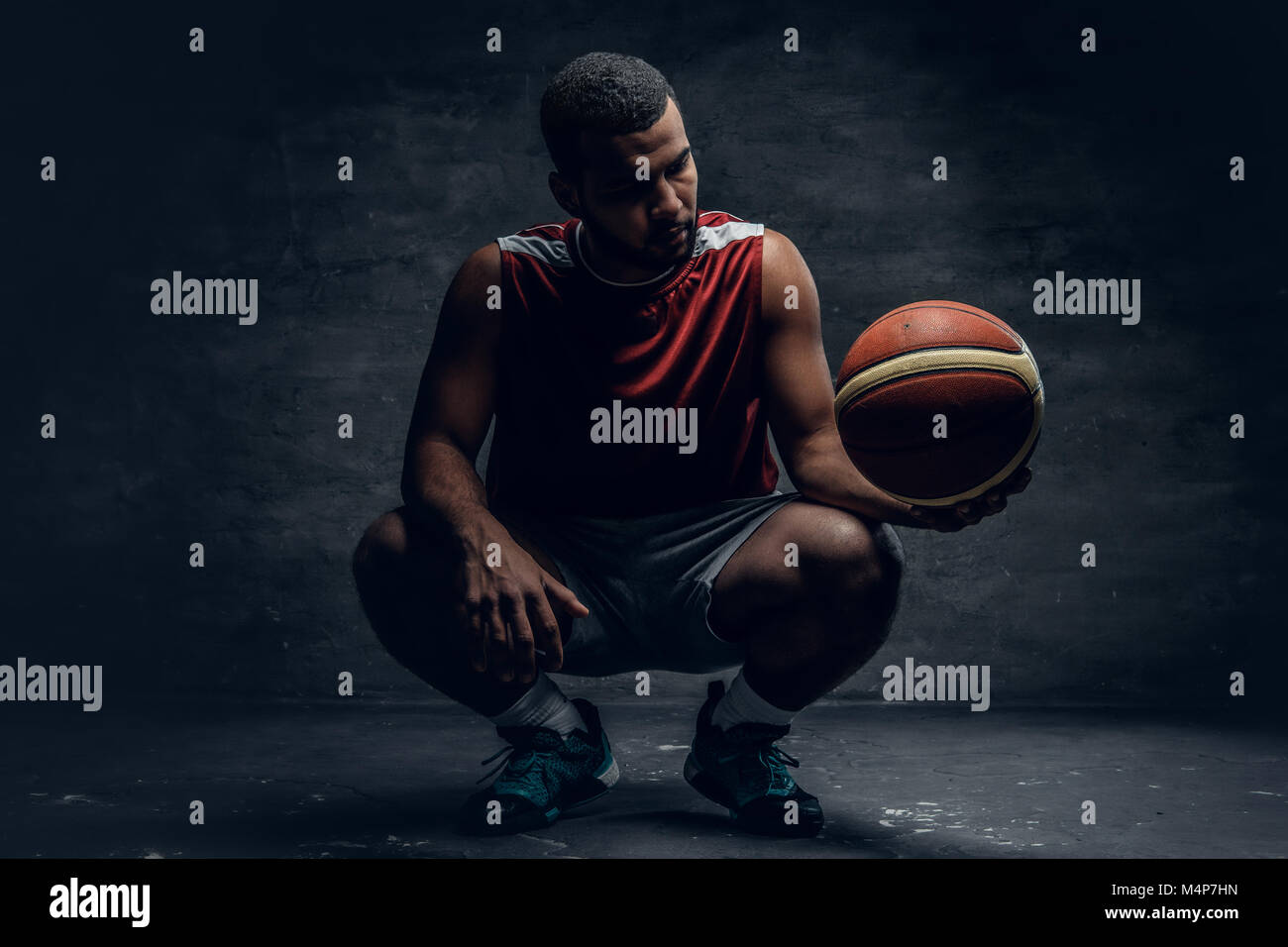 Full body portrait of a black basketball player sits on a floor and ...
