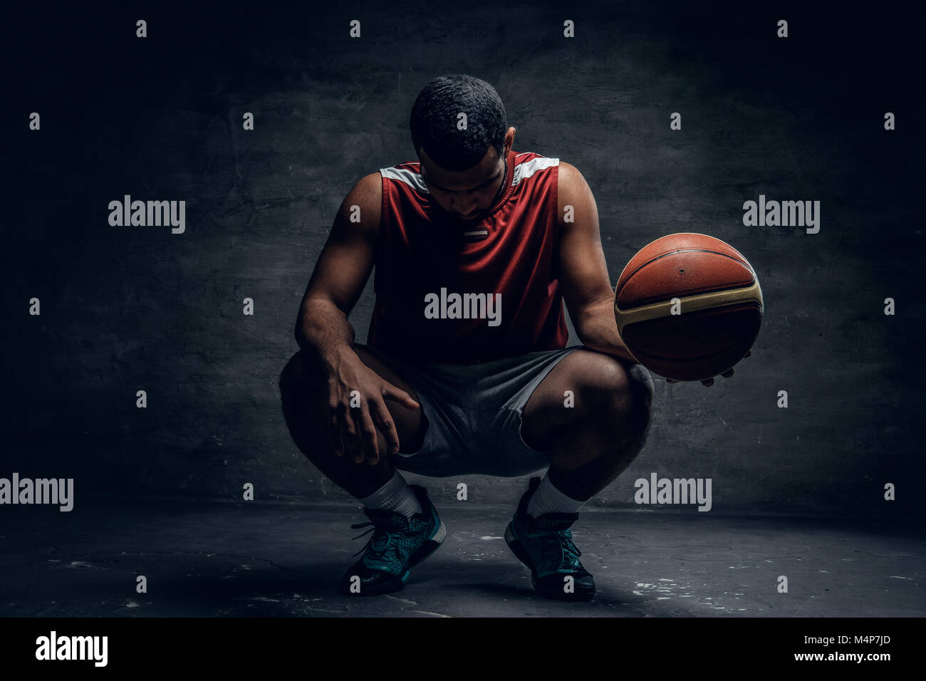 Full body portrait of a black basketball player sits on a floor and ...
