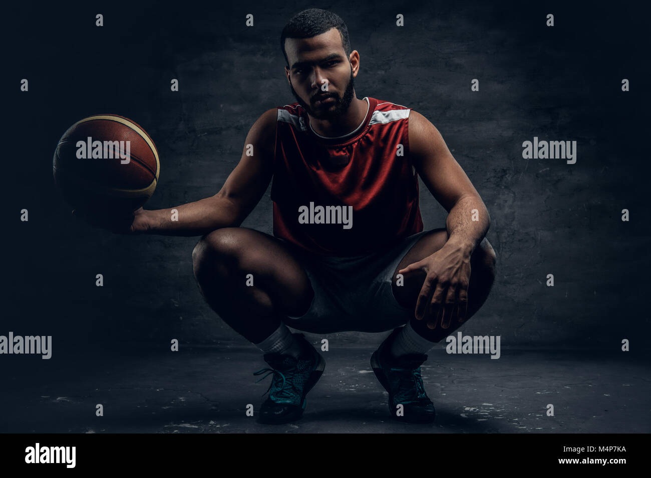 Full body portrait of a black basketball player sits on a floor and ...