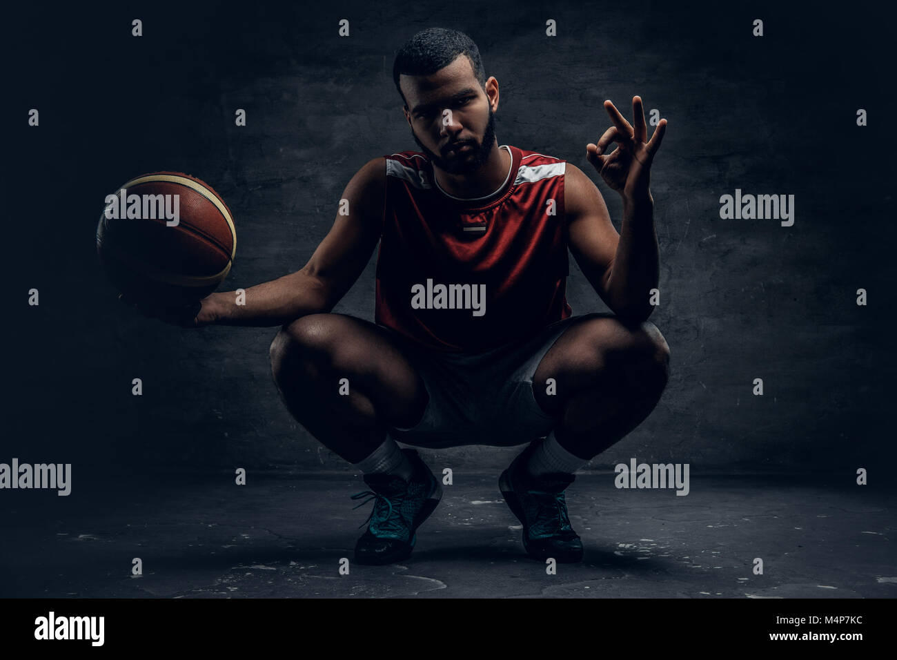 Full body portrait of a black basketball player sits on a floor and ...
