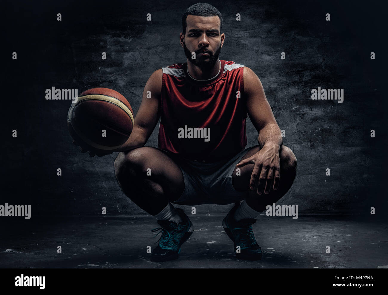 Full body portrait of a black basketball player sits on a floor and ...