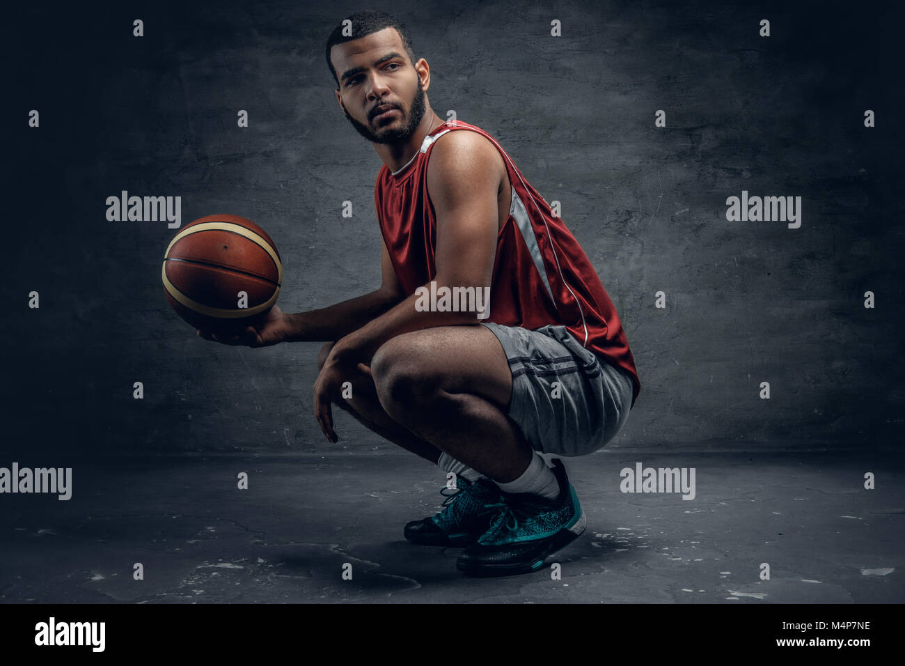 Full body portrait of a black basketball player sits on a floor and ...