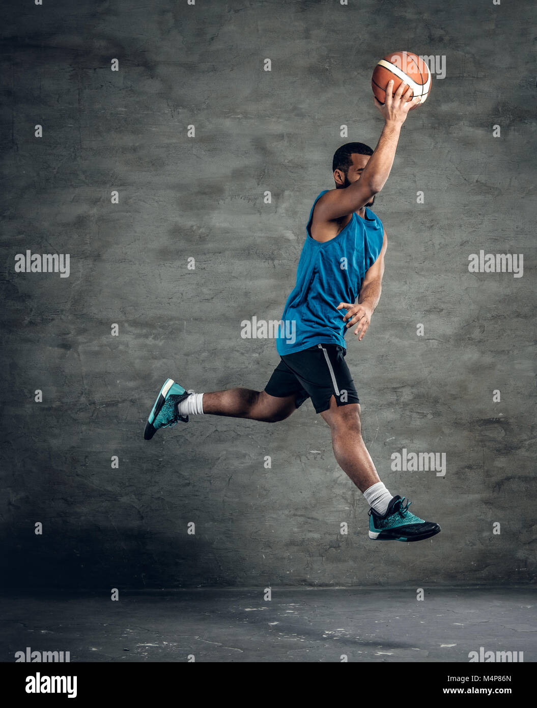 Jumping black man basketball player in a blue sportswear over grey ...