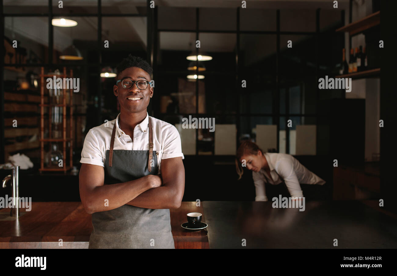 Man standing in his coffee shop with arms crossed while woman is ...