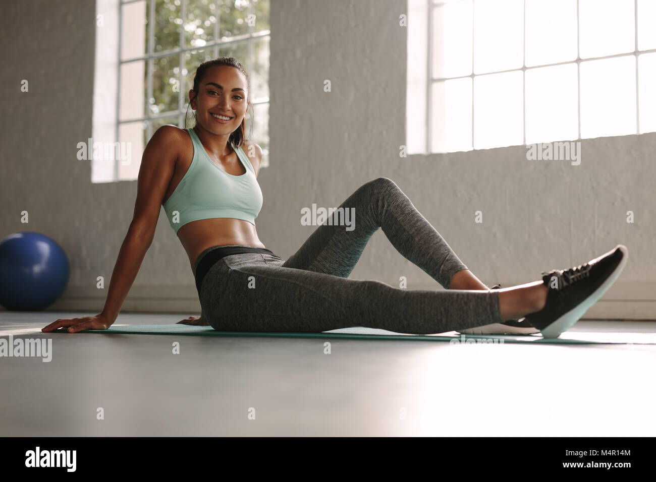 fitness woman smiling while resting on exercising mat at gym. Female ...