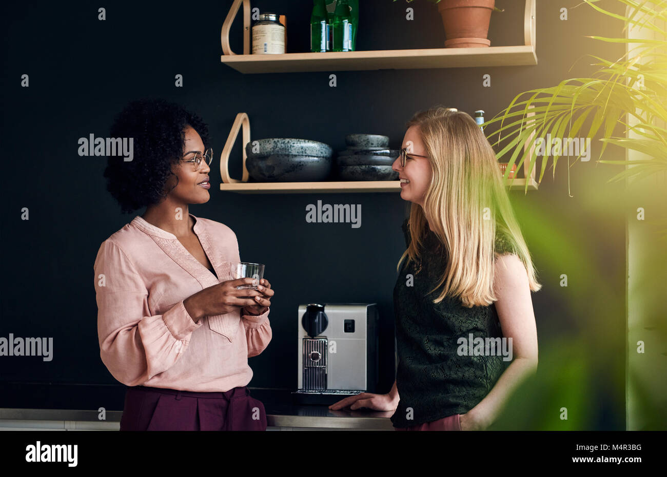 Two diverse female work colleagues smiling and talking while taking a ...