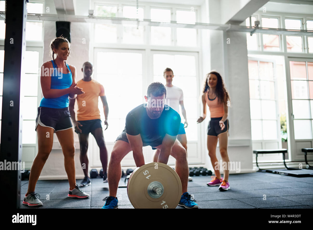 Young man straining to lift a barbell in a gym with a diverse group of ...