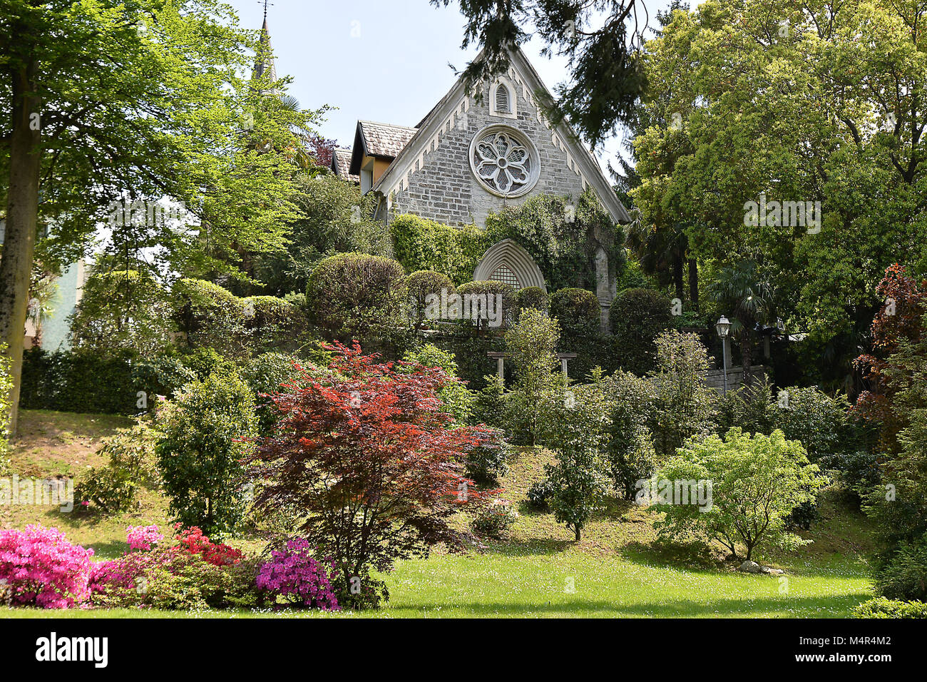 A beautiful old church in a rich garden with trees, flowers and ...