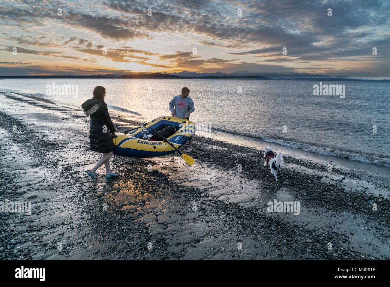 A couple launching an inflatable reft at sunset off Alki Beach, Seattle ...