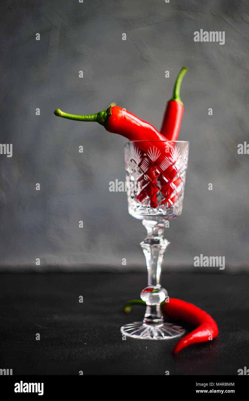 Crystal glass with red hot chilli pepper on dark table with copy space ...