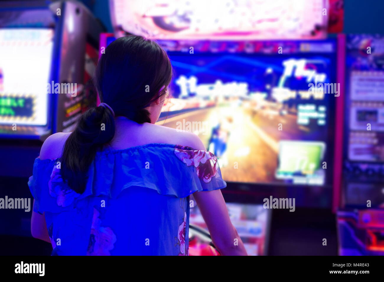 Girl playing in the arcade entertainment center rear view Stock Photo ...