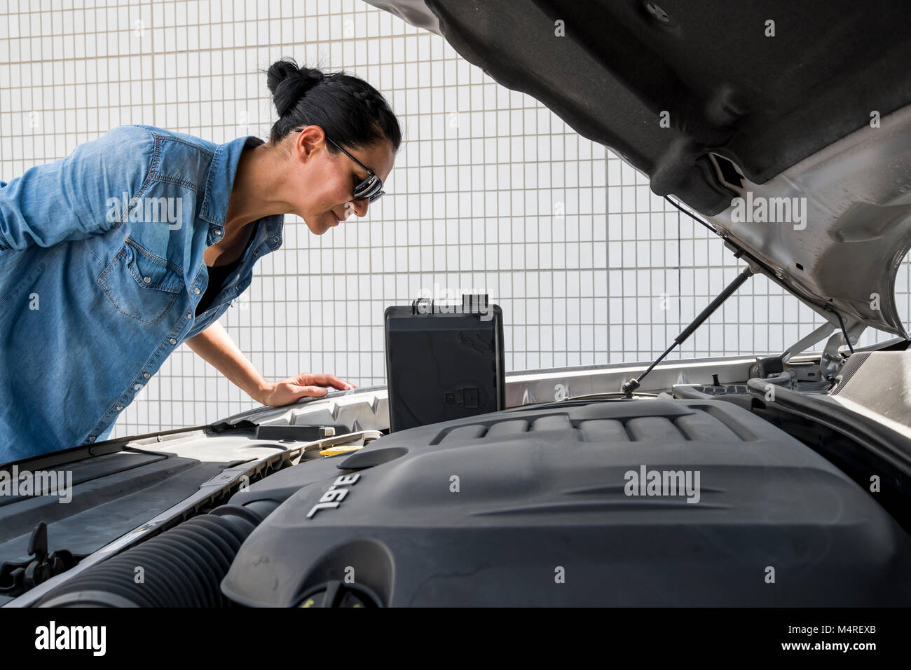 Focused woman inspecting the fuse box of her sports, searching for any ...