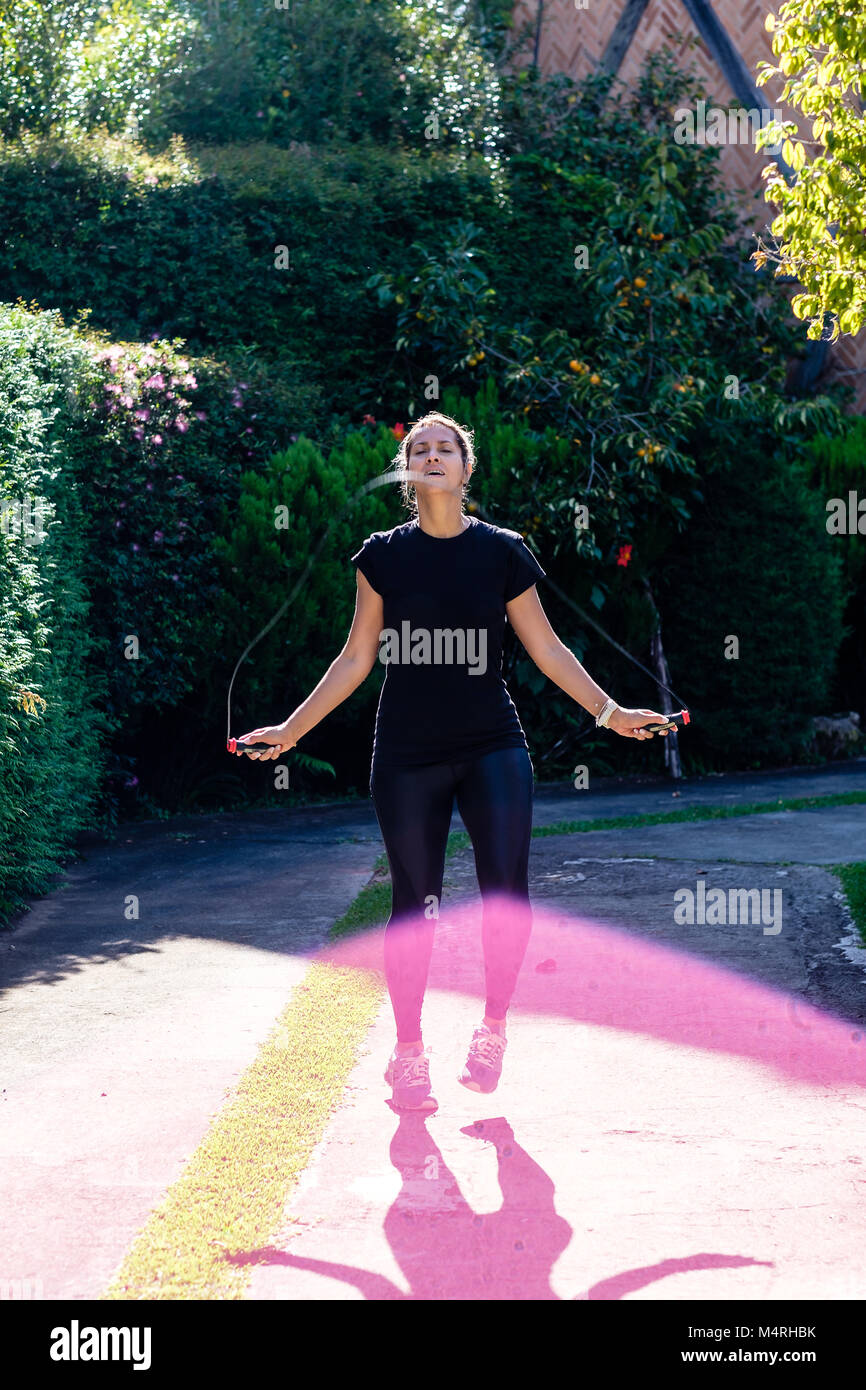 fit woman with black clothing jumping rope in the park under the sun ...