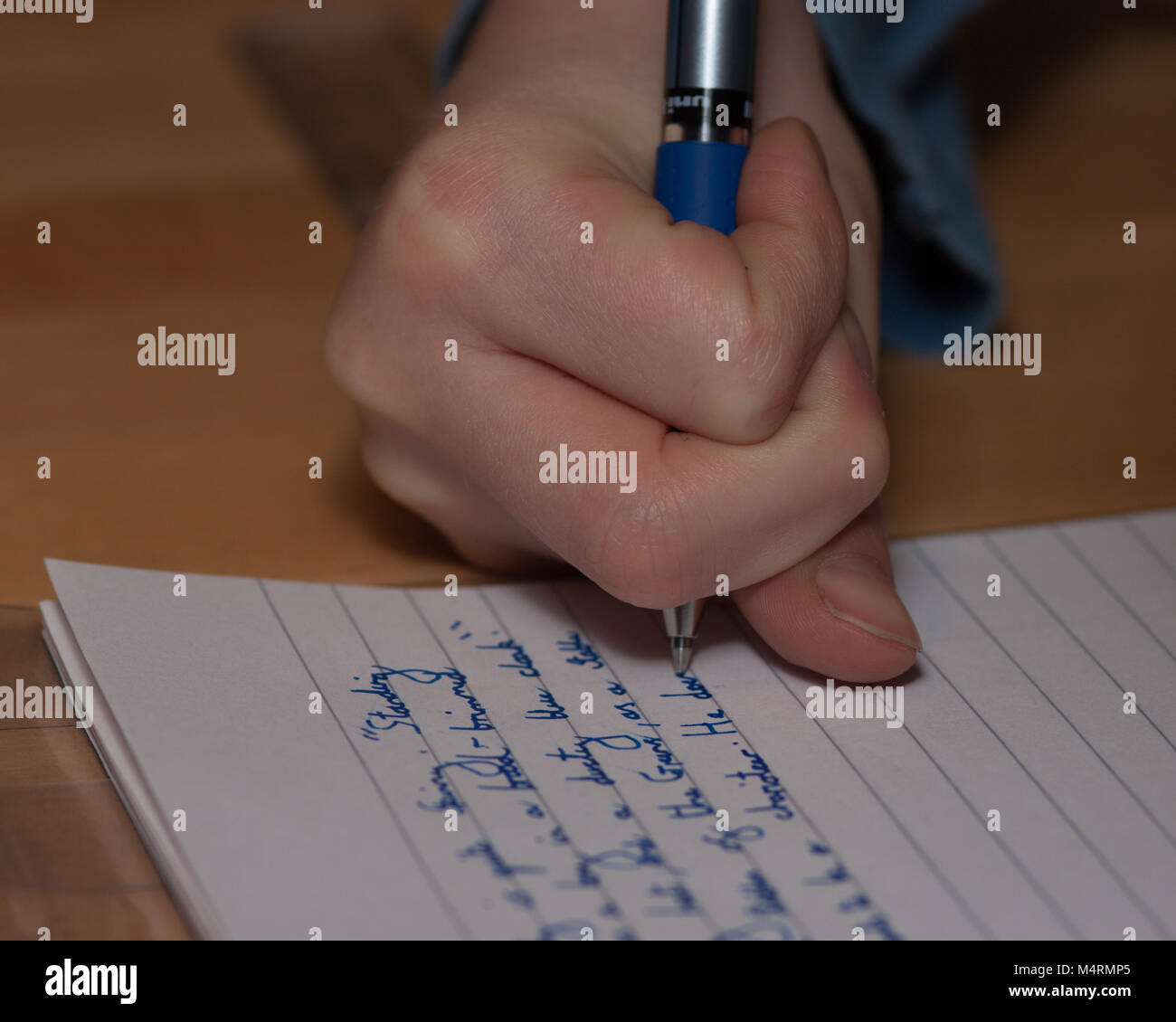 Child's hand practising writing on lined paper with blue pen Stock ...