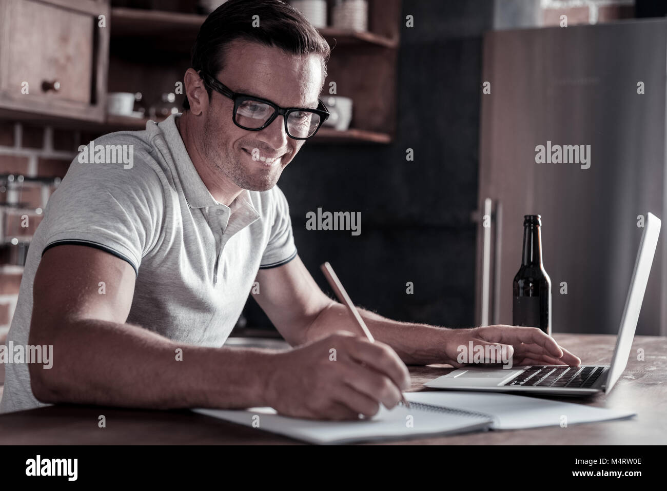 Joyful millennial guy taking notes while working on laptop Stock Photo ...