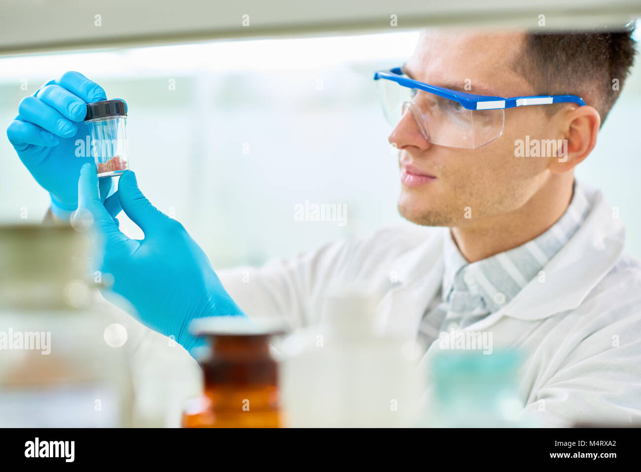 Concentrated young researcher wearing safety goggles and rubber gloves ...