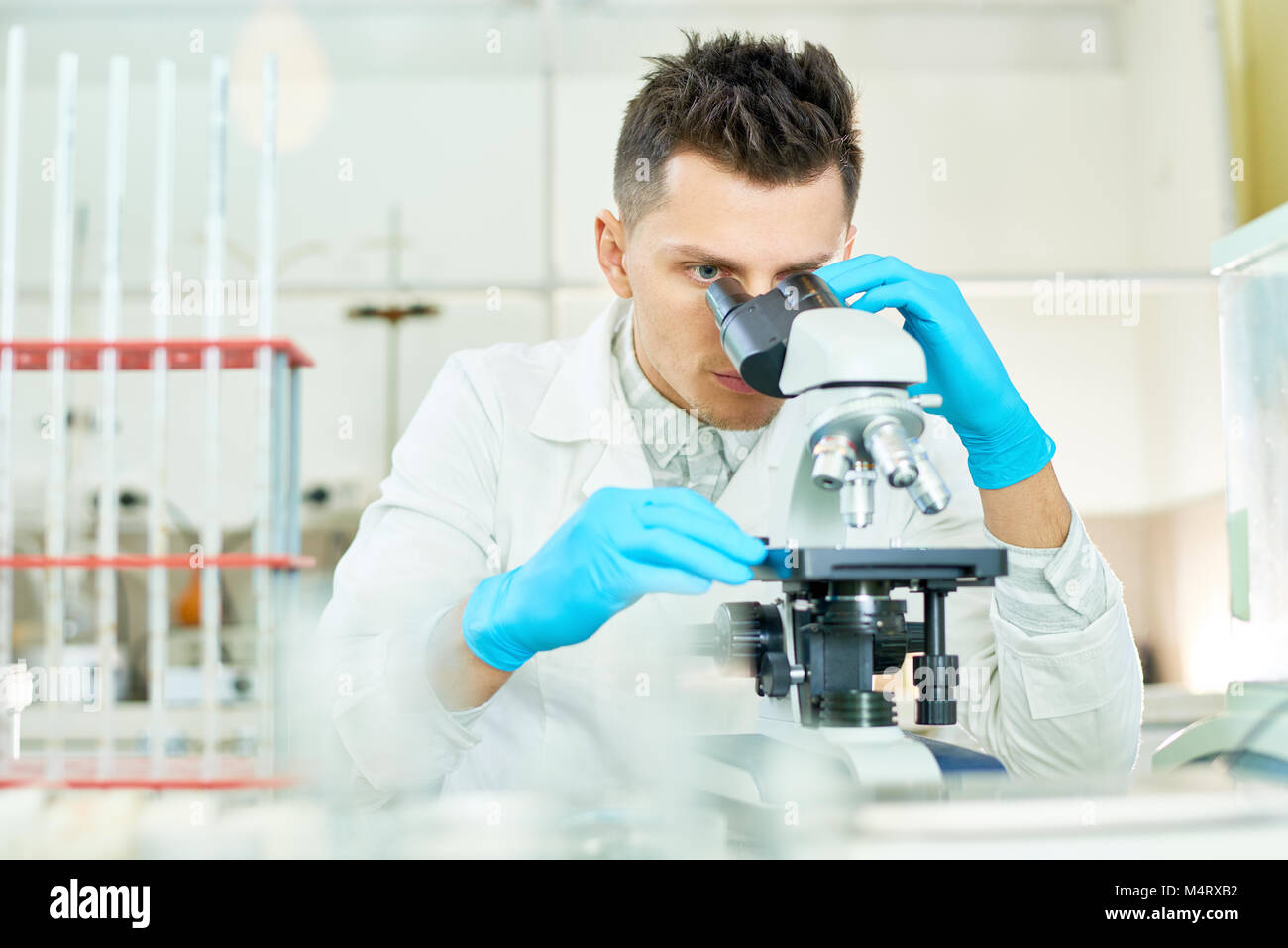 Portrait shot of concentrated young researcher wearing white coat and ...