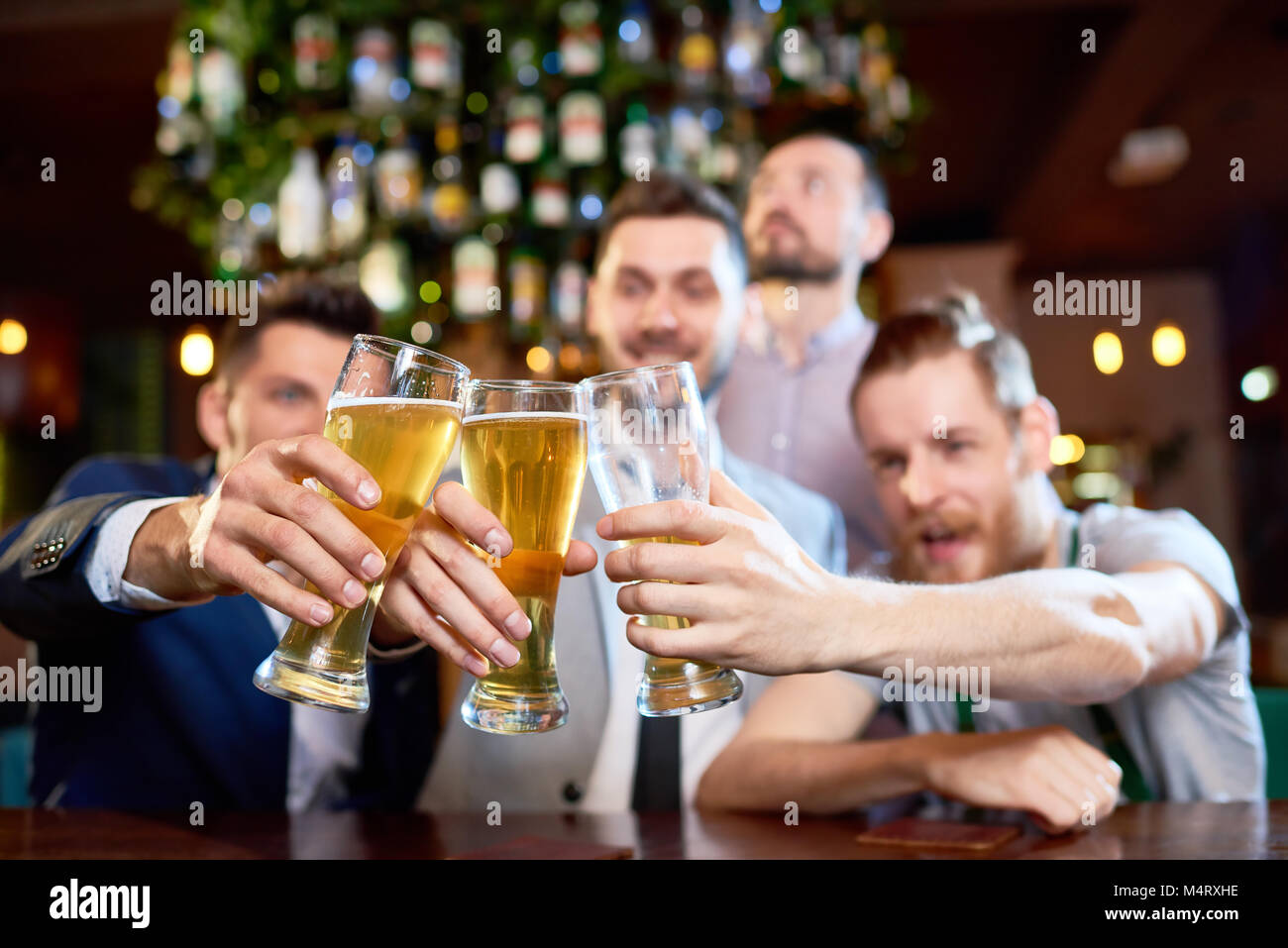 Group of cheerful friends clinking beer glasses together while sitting ...