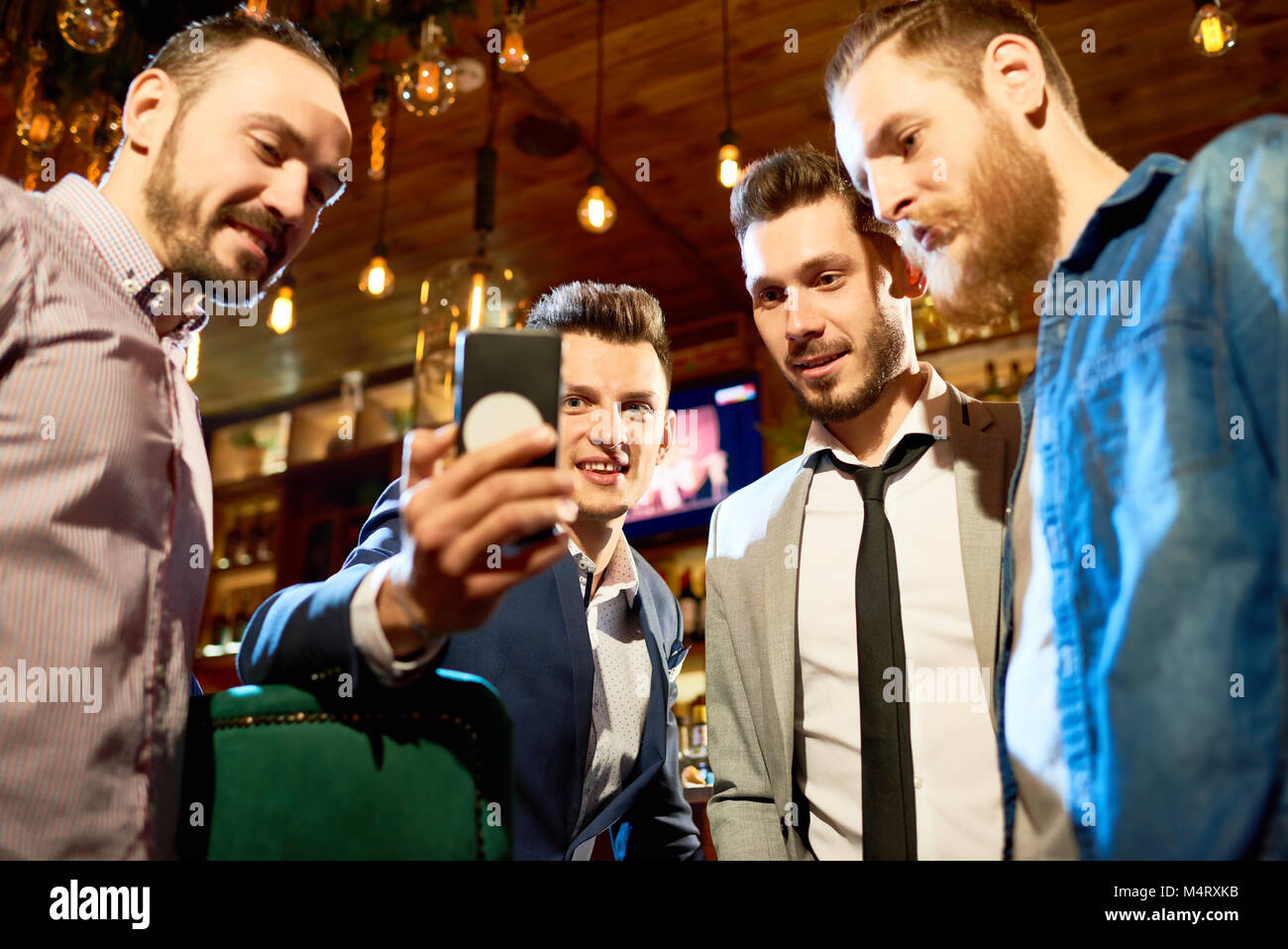 Low angle view of cheerful friends looking through funny photos on ...