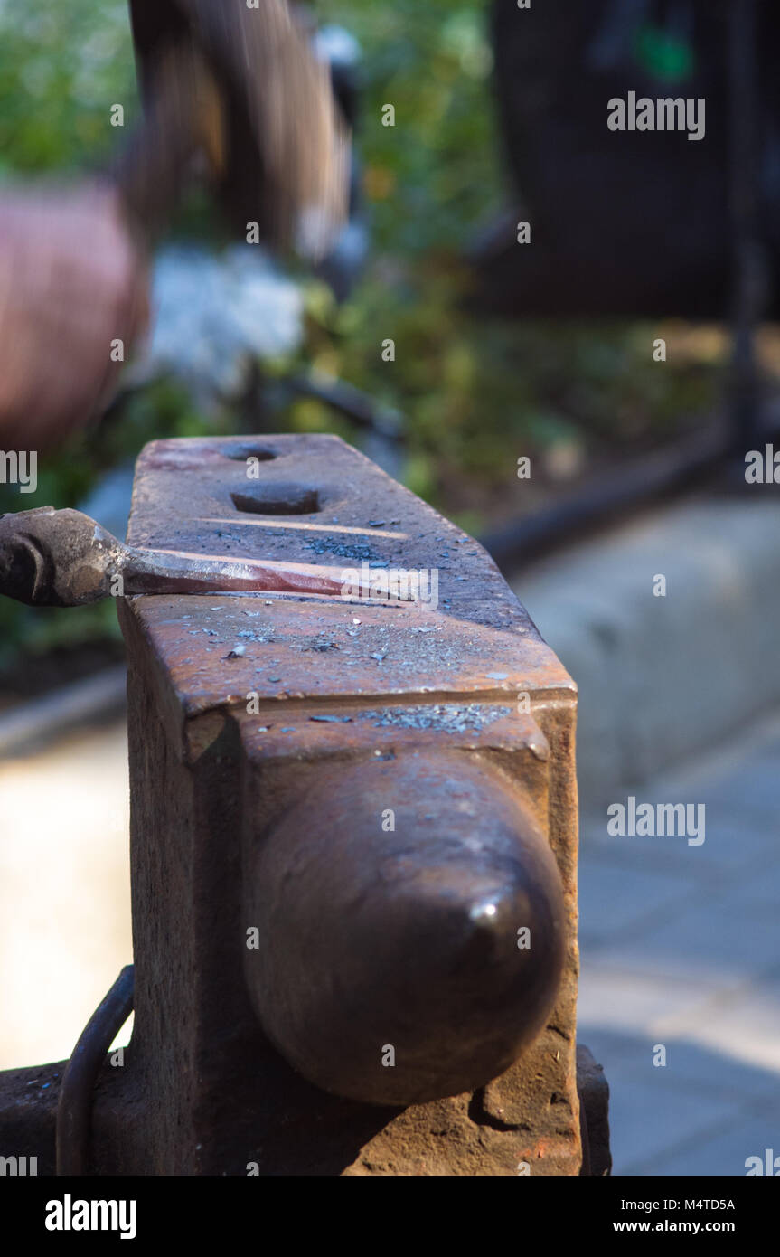 blacksmith performs the forging of hot glowing metal on the anvil ...