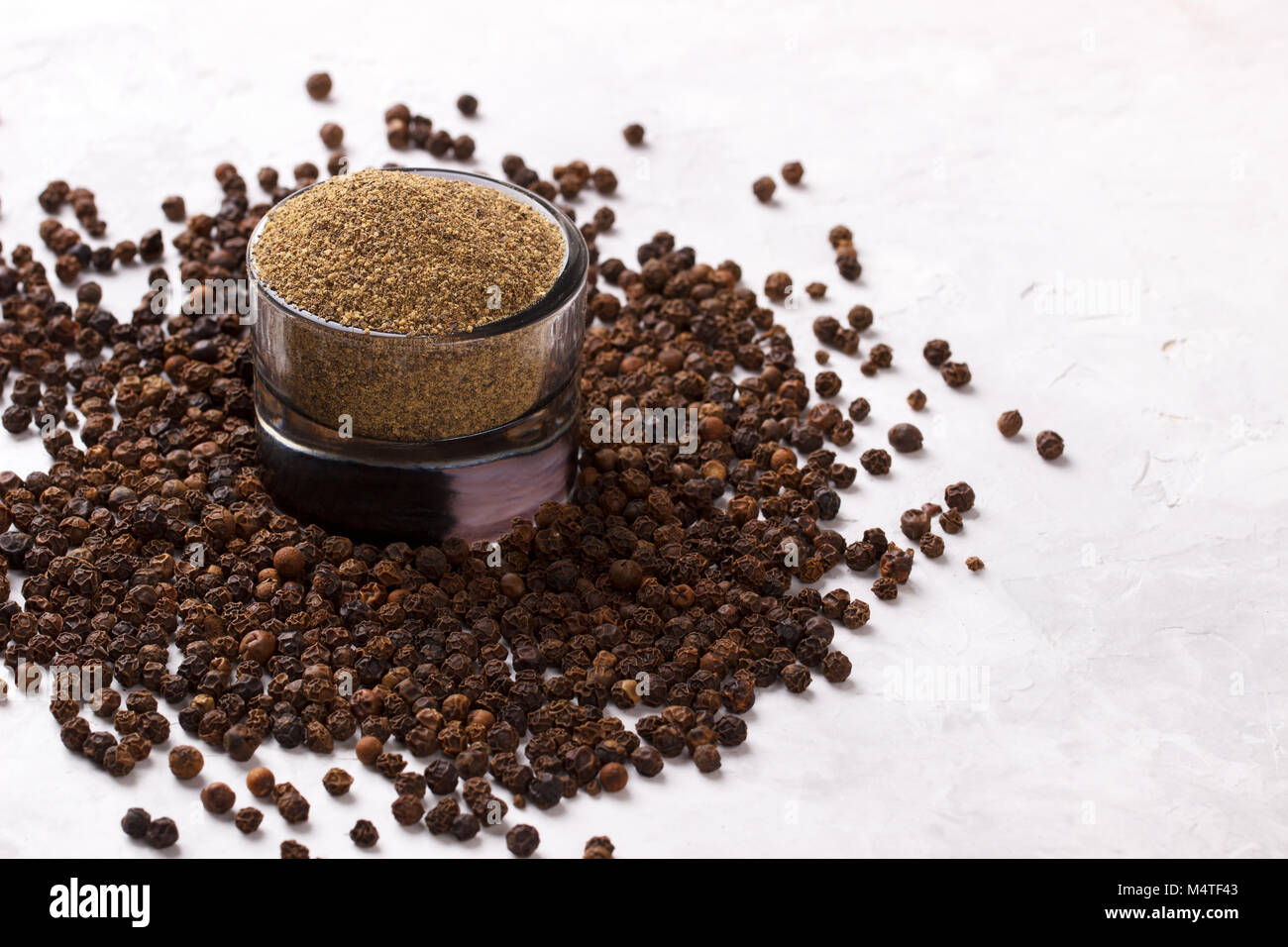 Black pepper corns and powder on white stone background, top view with ...