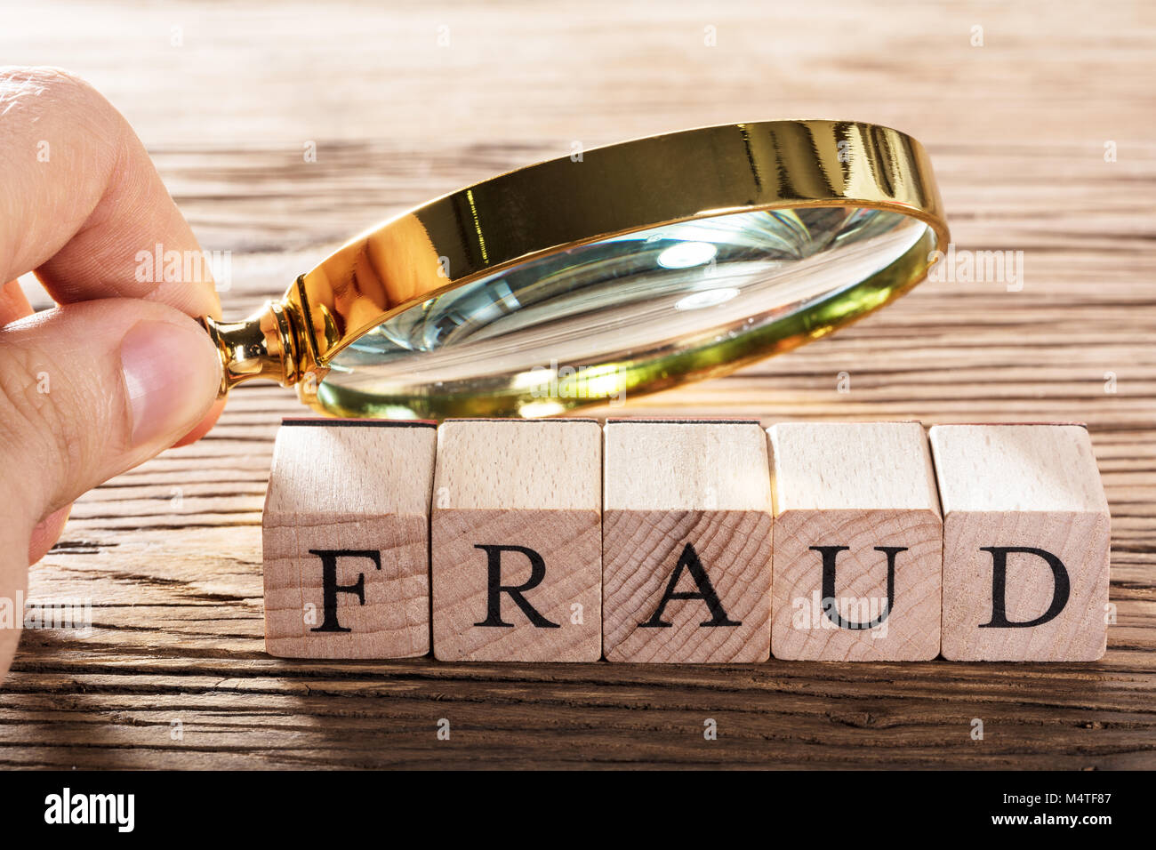A Person Examining Fraud Blocks Through Magnifying Glass On Wooden ...